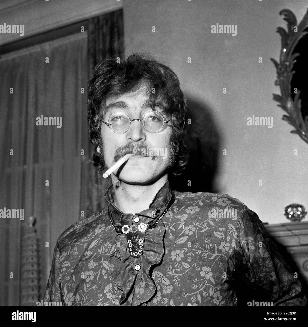 With drooping moustache , thin - rimmed specs , floral shirt and ...