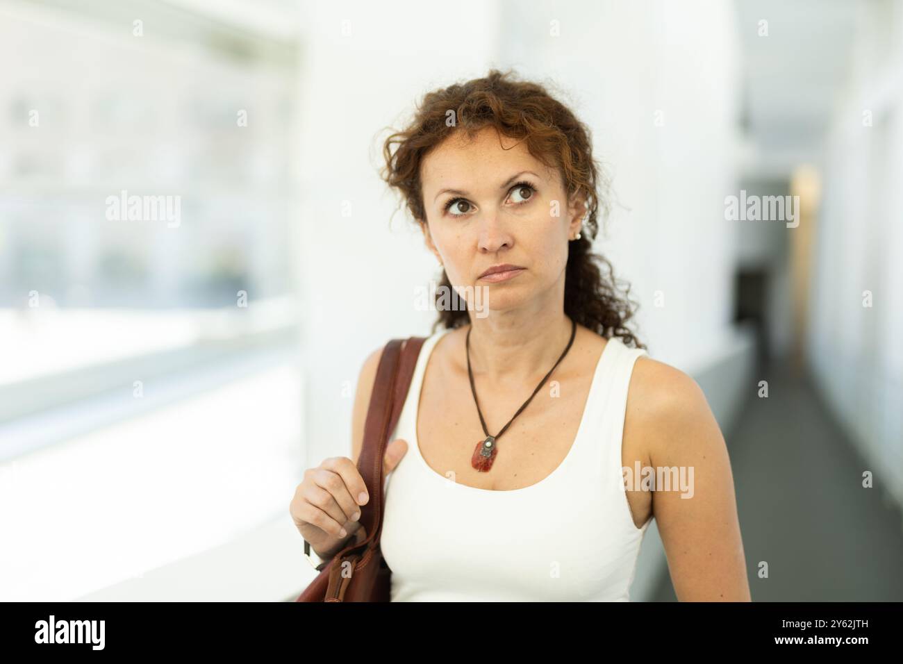 Middle-aged woman walking alone through corridor with wide windows ...