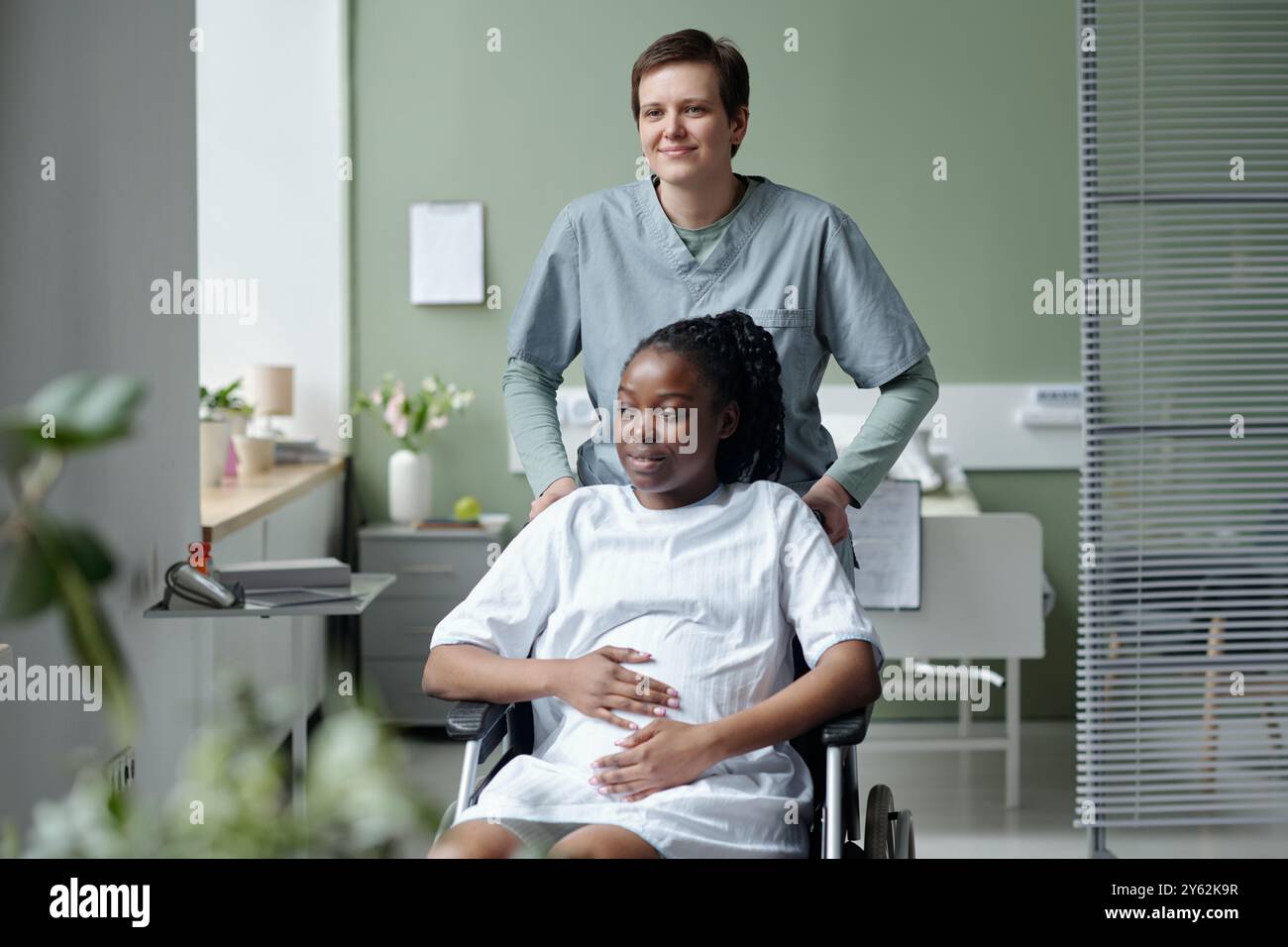 Smiling patient sitting in wheelchair in a hospital room with nurse ...