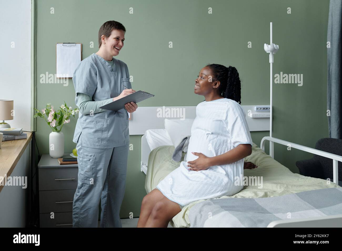 Nurse standing by hospital bed while engaging with pregnant African ...