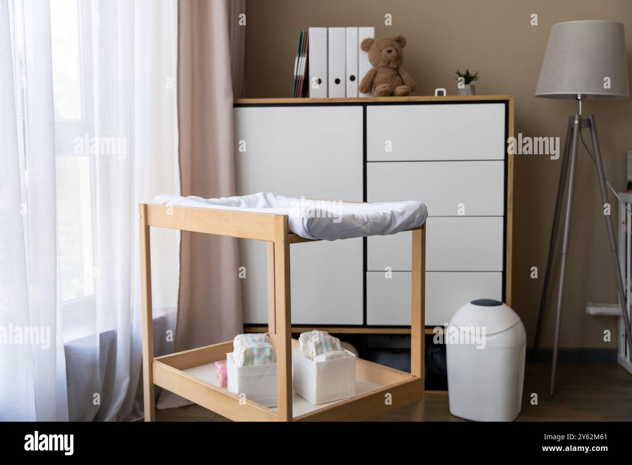 Empty nursery with changing table with diapers, lamp, commode and ...