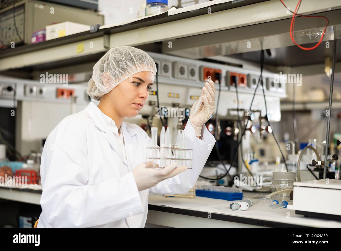 Skilled young female biochemist holding tripod and examining solution ...