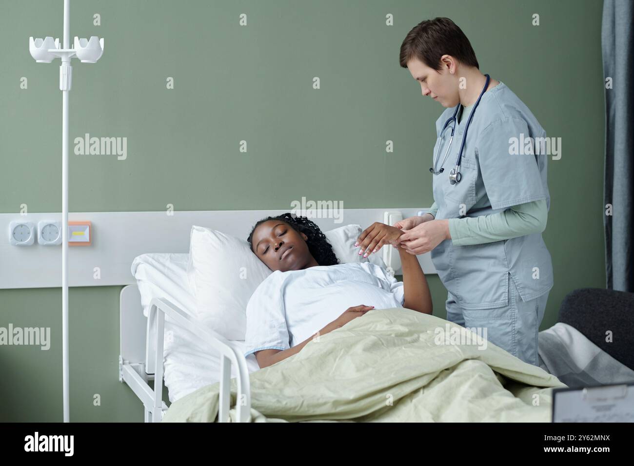Nurse holding patient hand and checking on resting patient in hospital ...