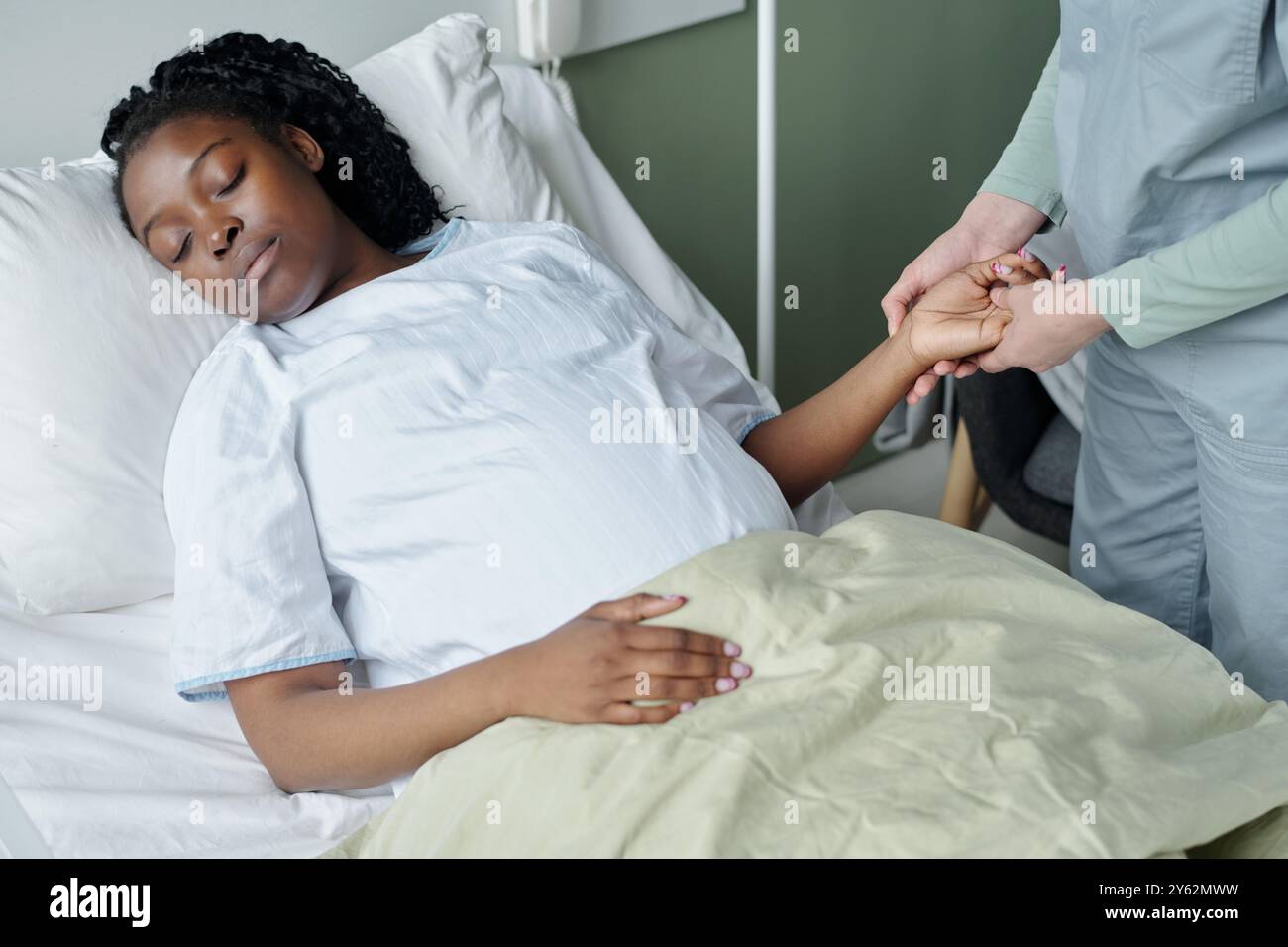 Nurse holding hands with a resting patient in hospital bed providing ...