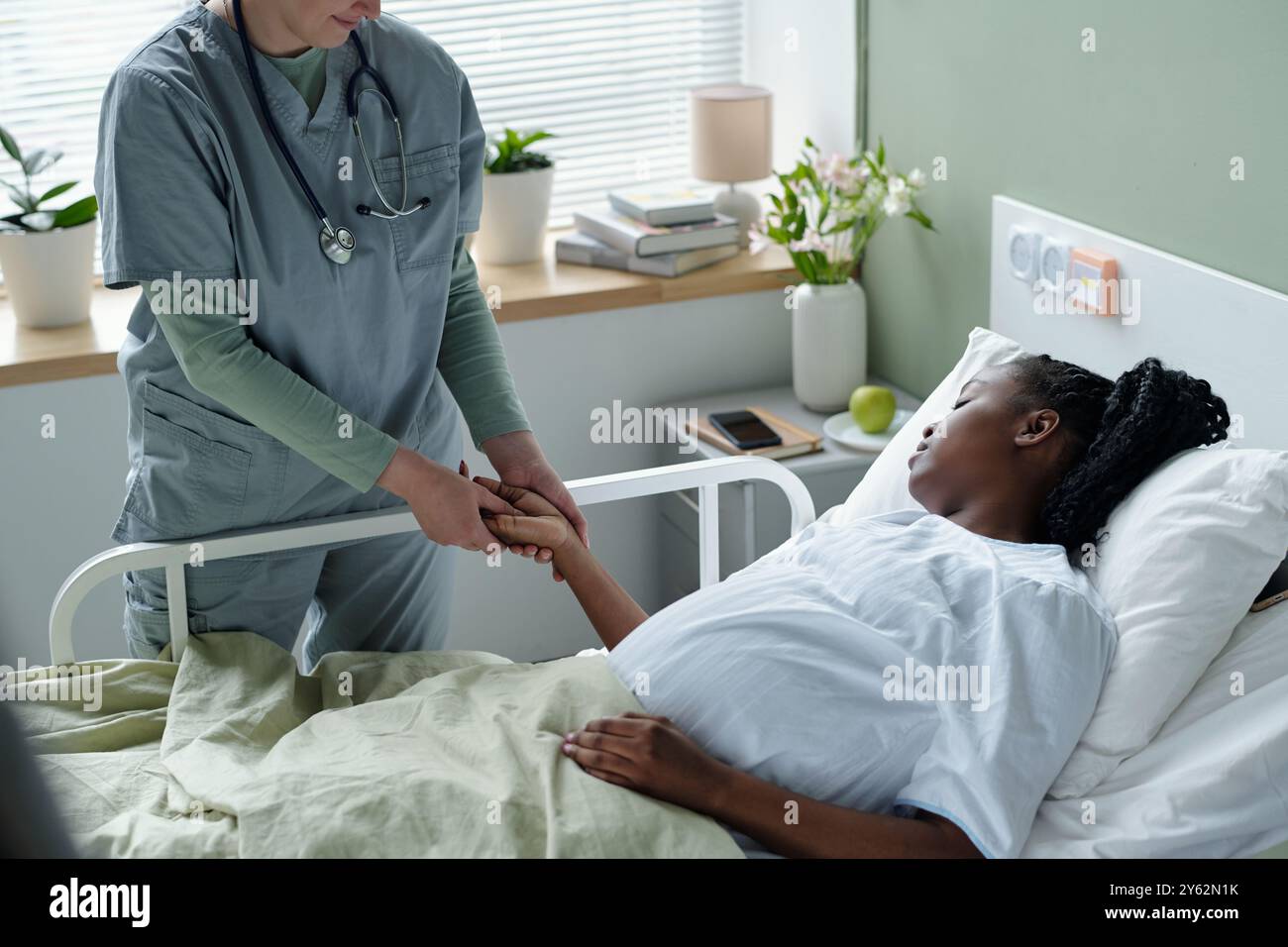 Nurse standing beside hospital bed, holding patient's hand while ...