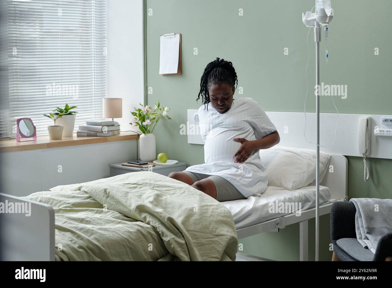 Person recovering and sitting on hospital bed with IV drip by side in a ...