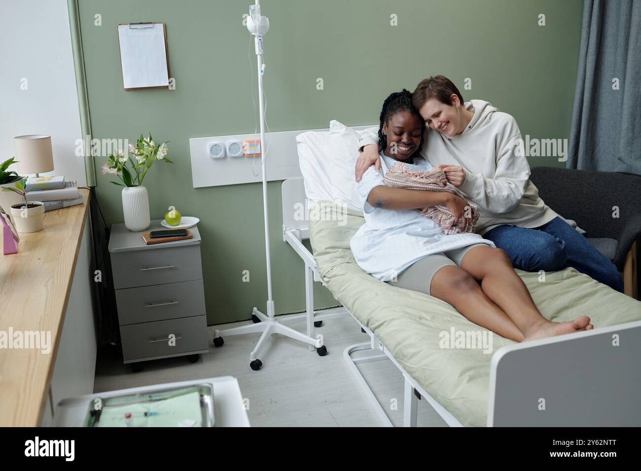 Friend comforting woman in hospital bed, sitting on side of bed and ...