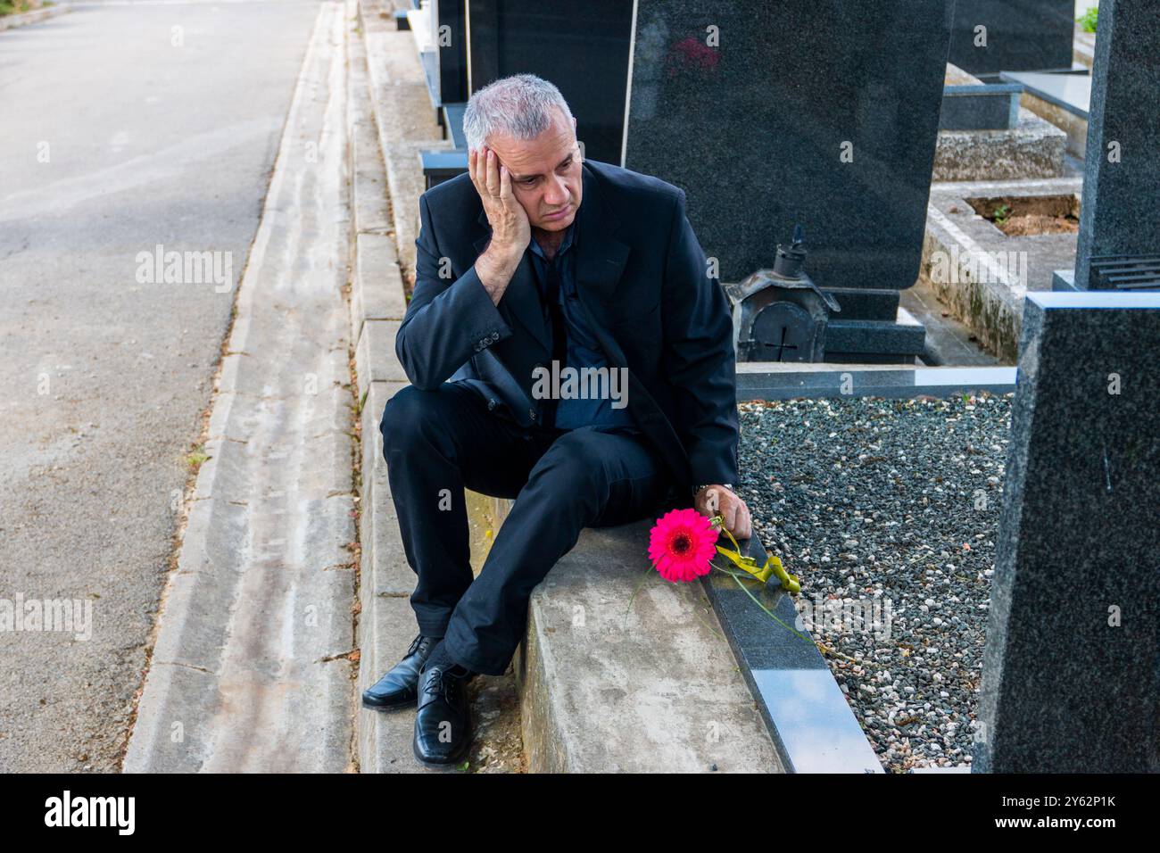 Mature man in black clothes on cemetery, holding a flower and mourning ...