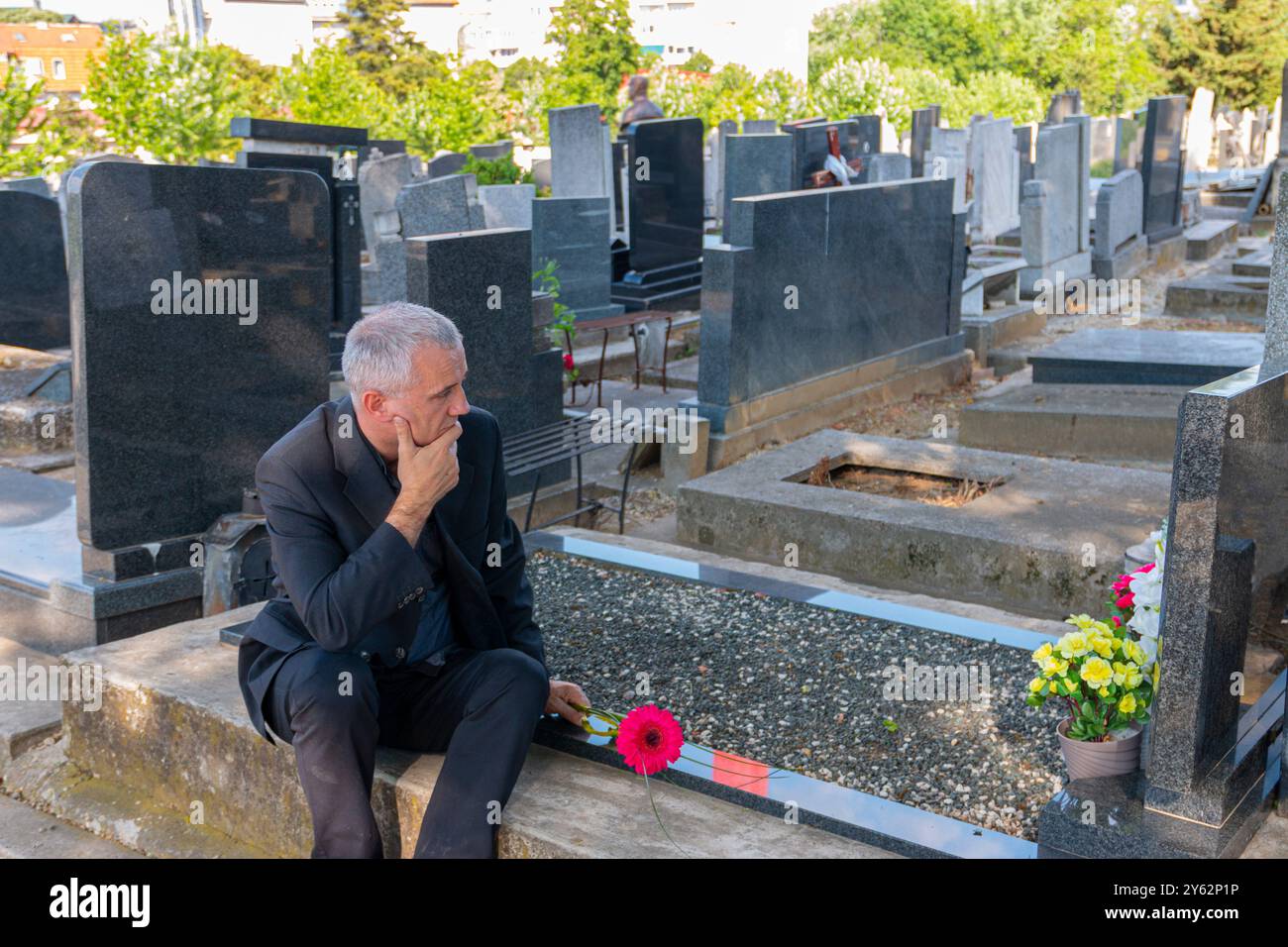 Mature man in black clothes on cemetery, holding a flower and Mourning ...