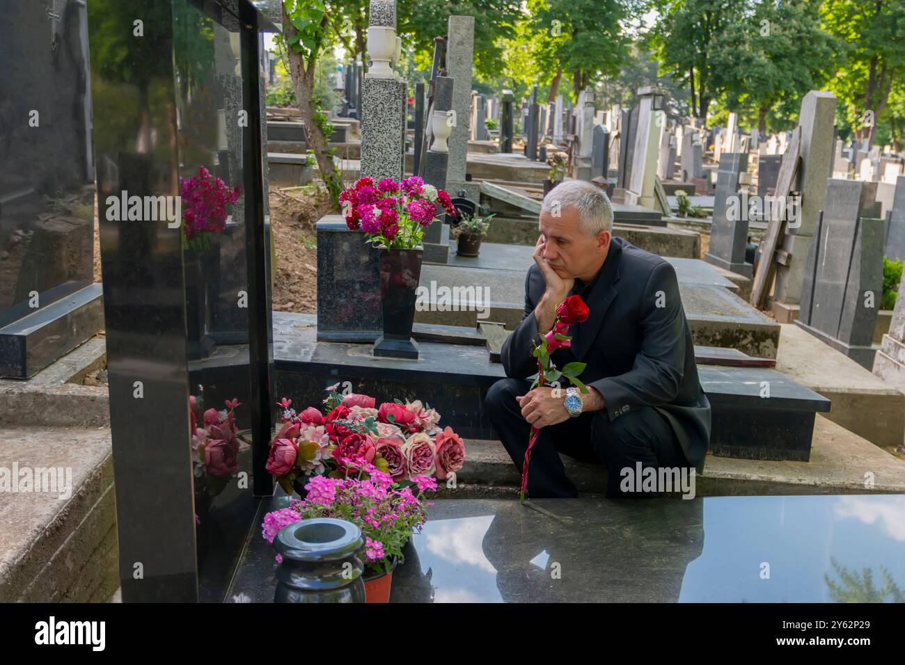 Mature man in black clothes on cemetery, holding a flower and Mourning ...