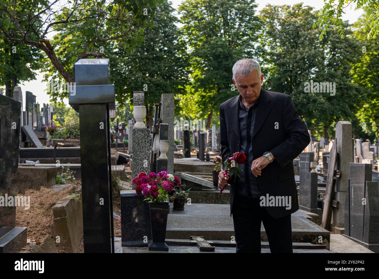 Mature man in black clothes on cemetery, holding a flower and mourning ...