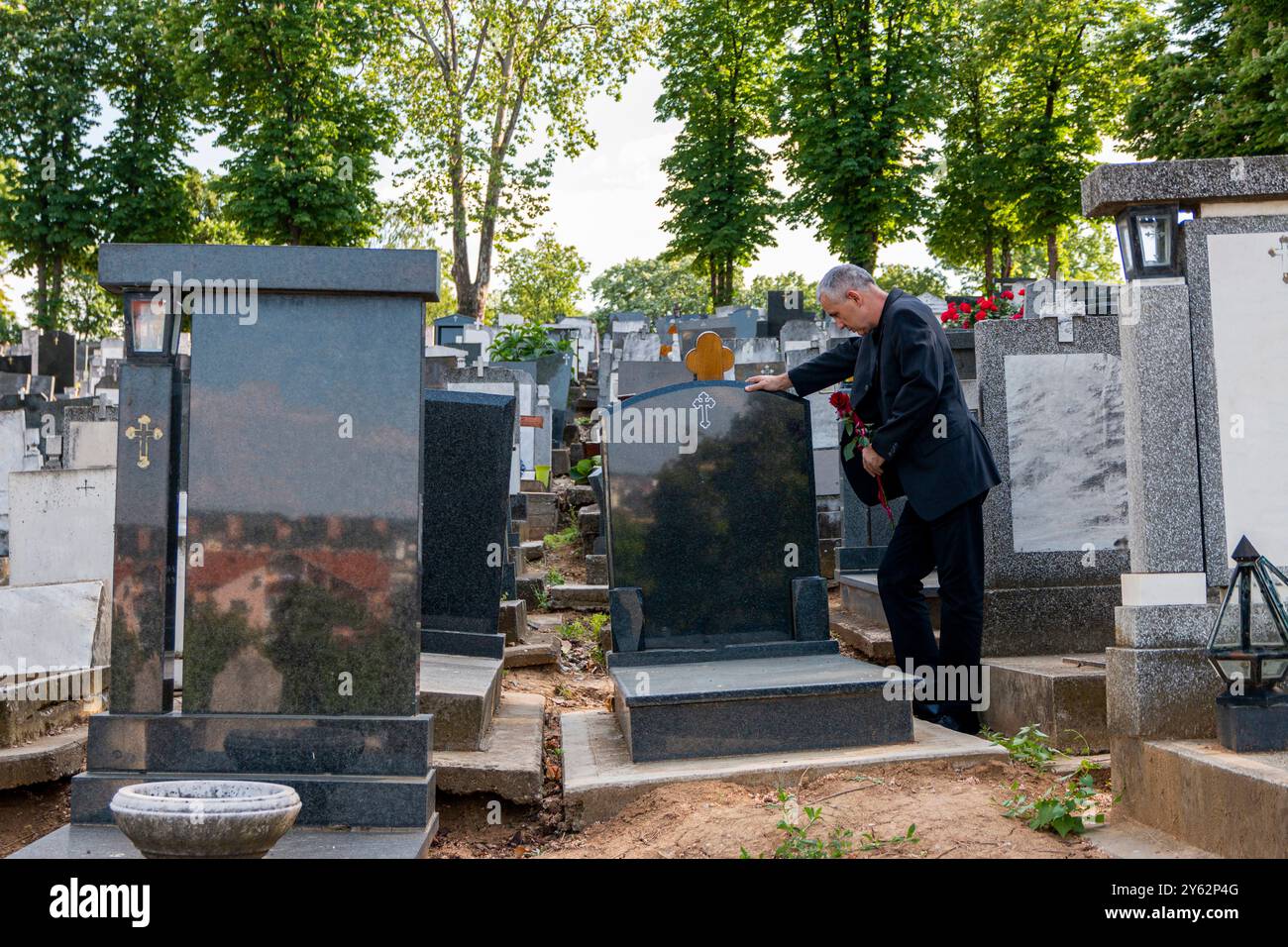Mature man in black clothes on cemetery, holding a flower and mourning ...