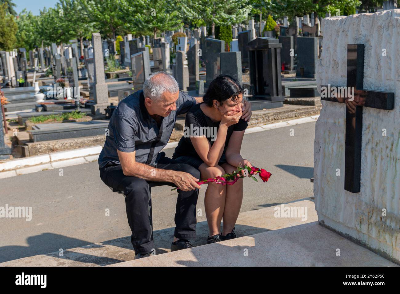 Mature couple in grief, in black clothes, holding a flower and mourning ...