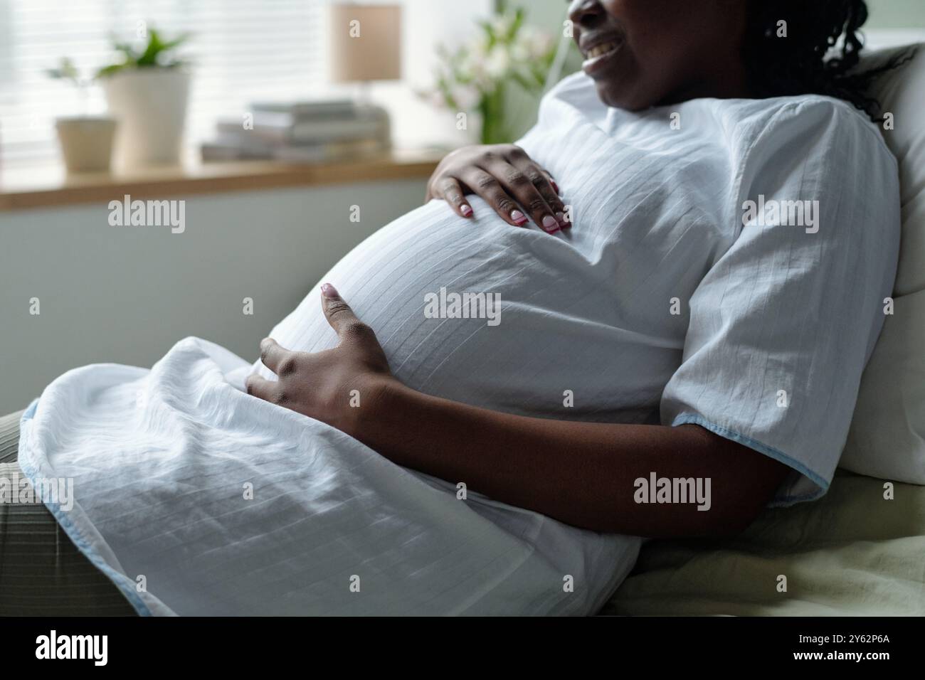 African American expecting mother sitting comfortably on couch, holding ...