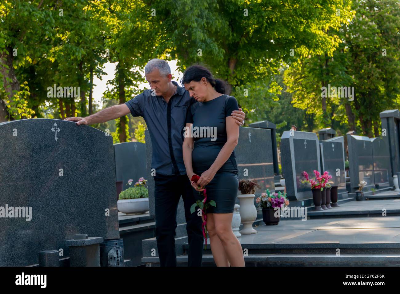 Mature couple in grief, in black clothes, holding a flower and mourning ...