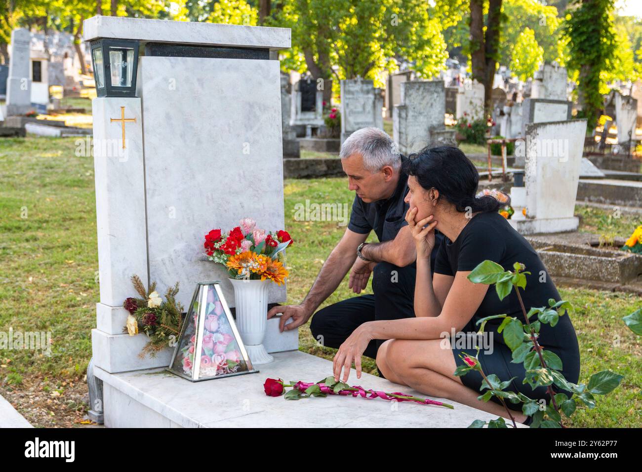 Mature couple in grief, in black clothes, holding a flower and mourning ...