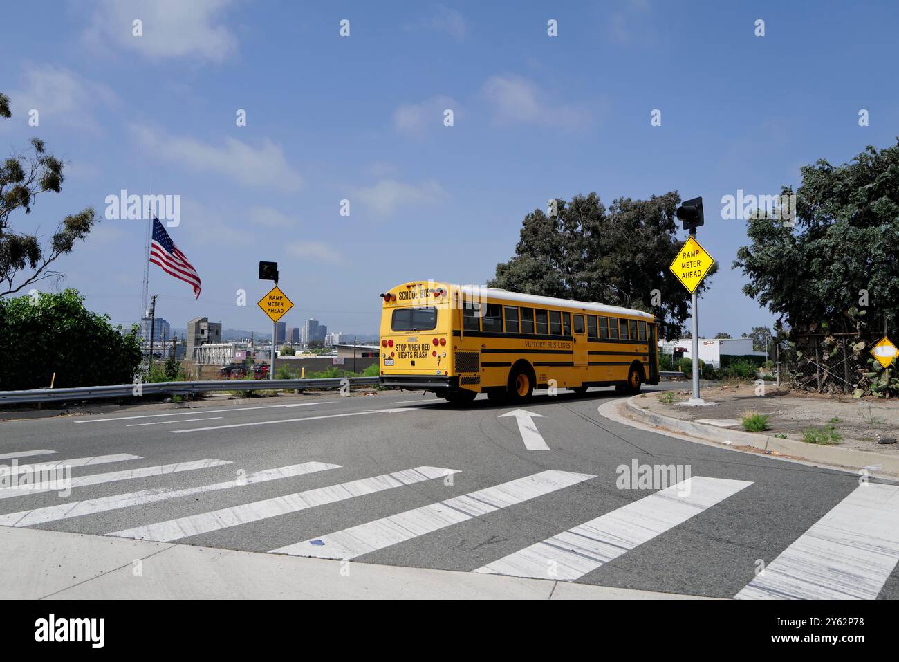 A yellow school bus navigates an urban road near a city skyline, with ...