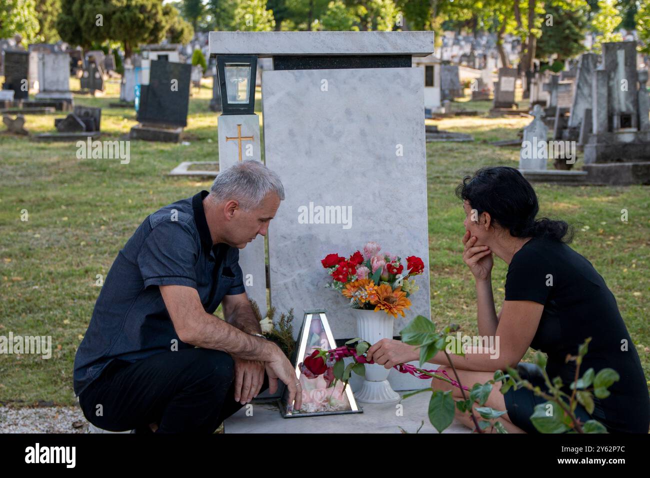 Mother and her daughter in grief, in black clothes, holding a flower ...