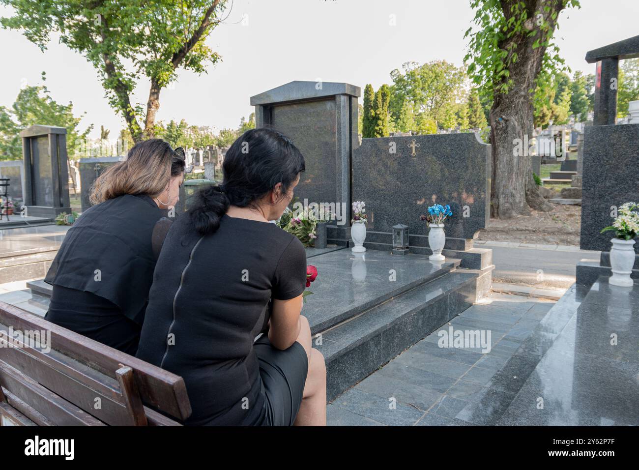 Mother and her daughter in grief, in black clothes, holding a flower ...