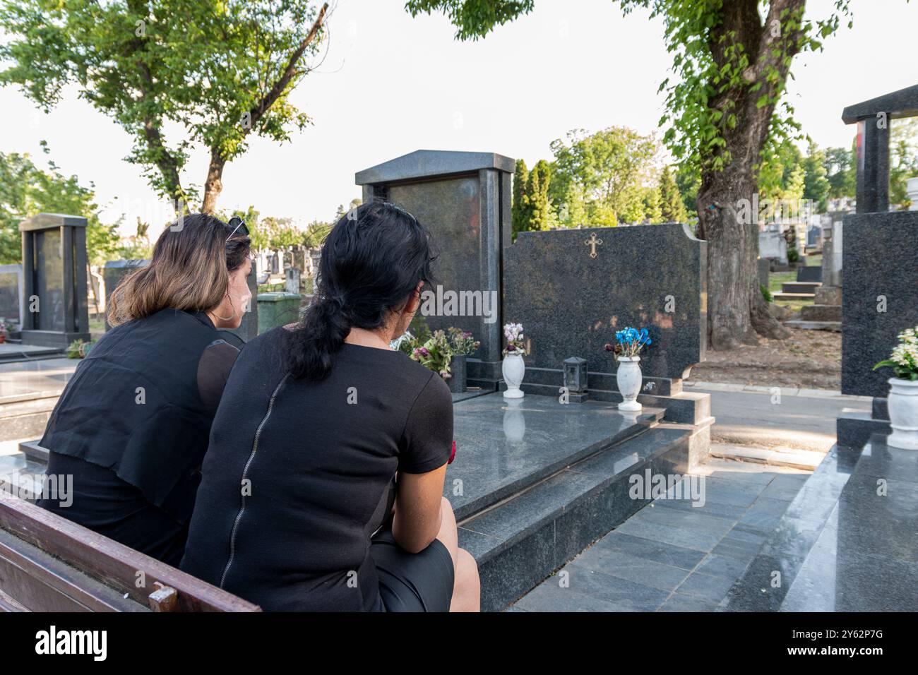 Mother and her daughter in grief, in black clothes, holding a flower ...