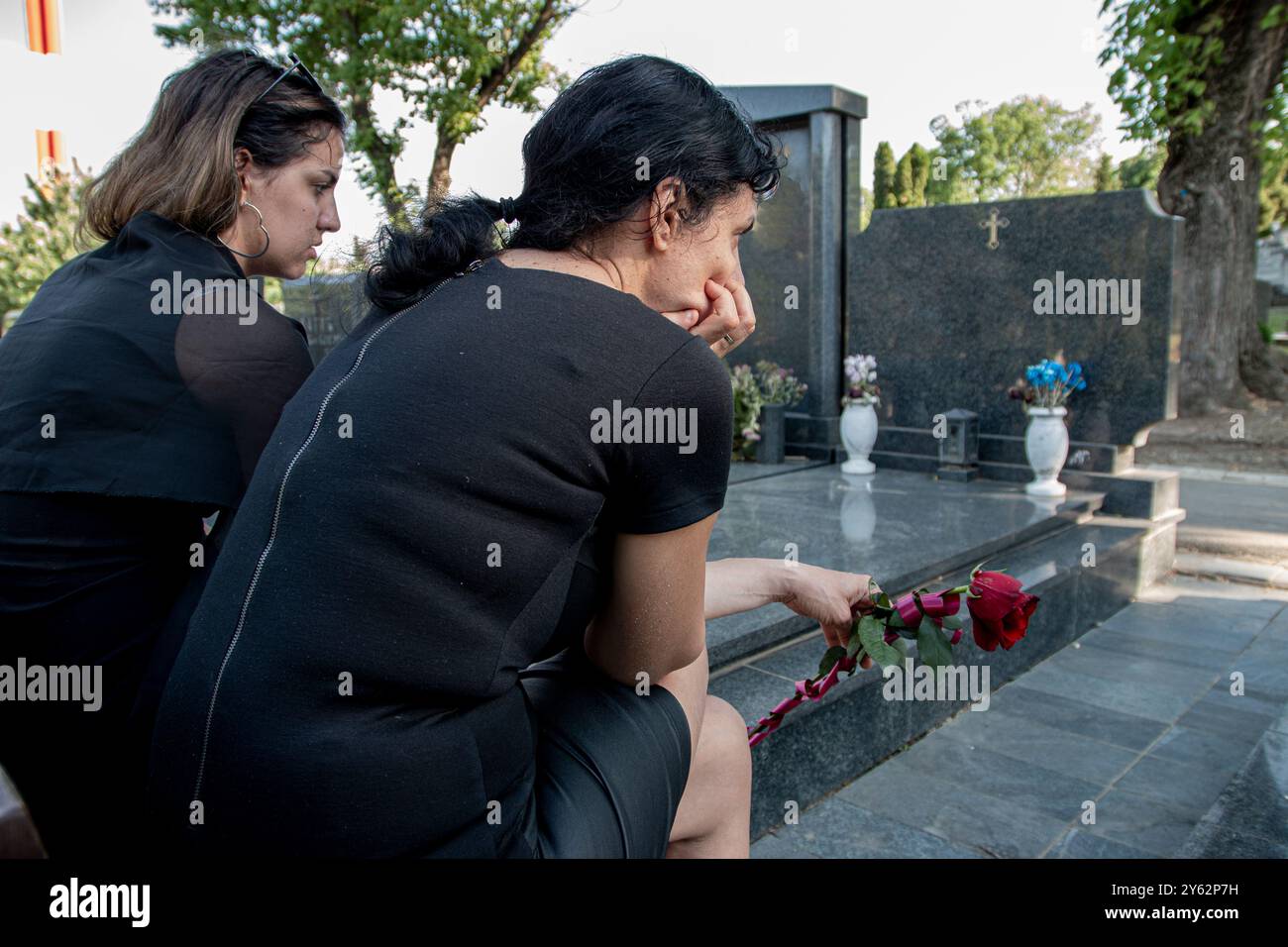 Mother and her daughter in grief, in black clothes, holding a flower ...