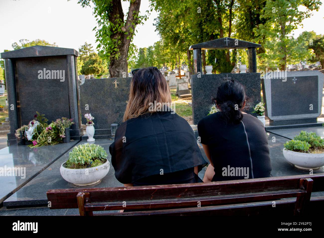 Mother and her daughter in grief, in black clothes, holding a flower ...