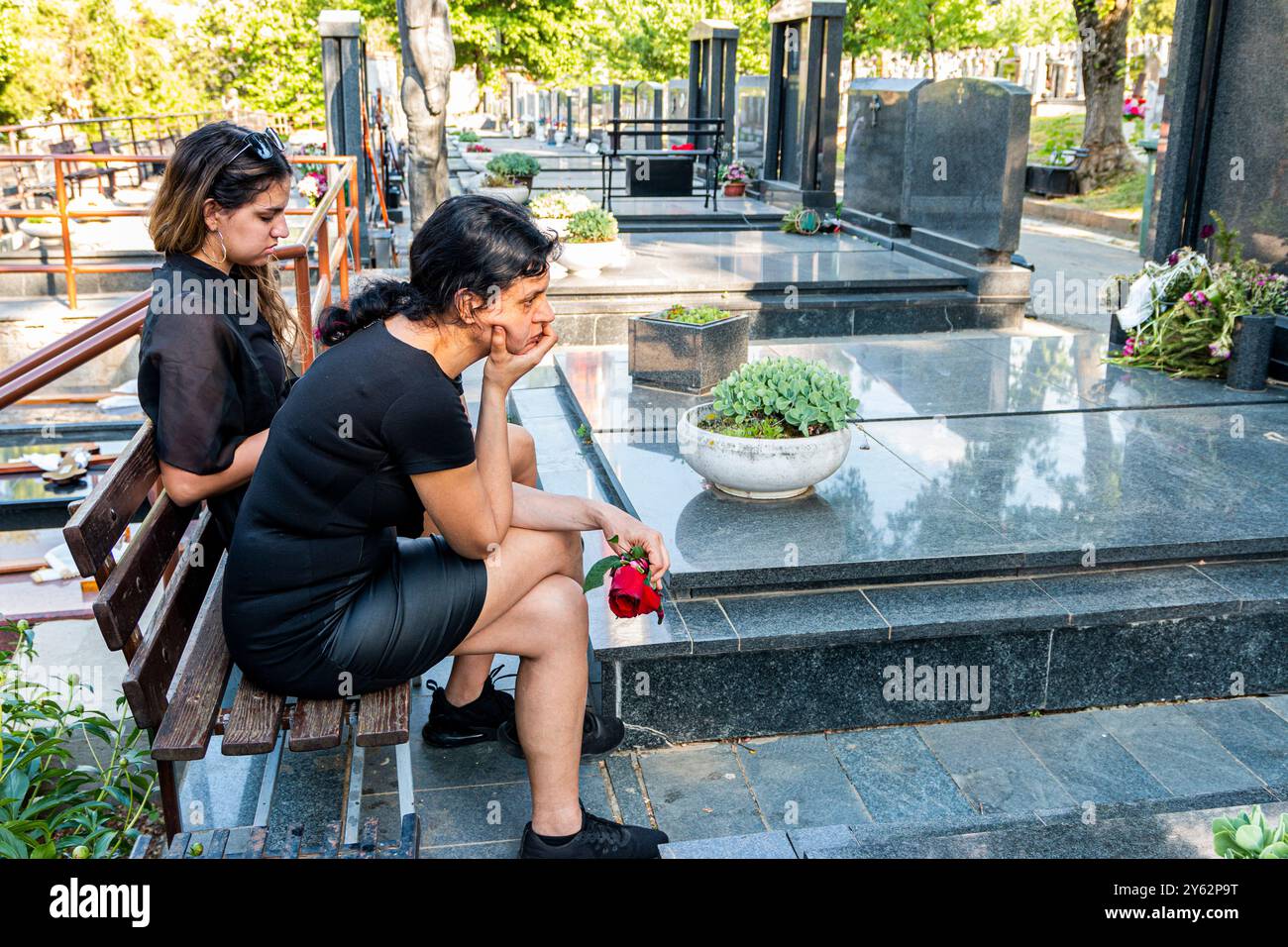 Mother and her daughter in grief, in black clothes, holding a flower ...