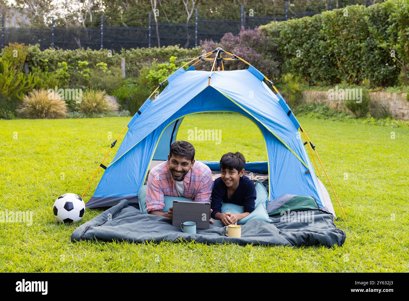 Camping in backyard, Indian father and son watching tablet inside tent ...