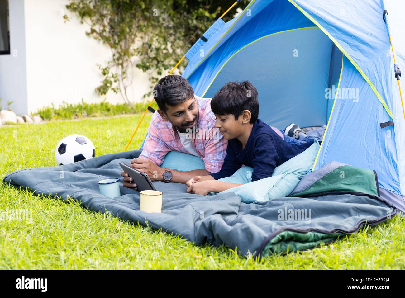 Camping in backyard, Indian father and son using tablet inside tent ...