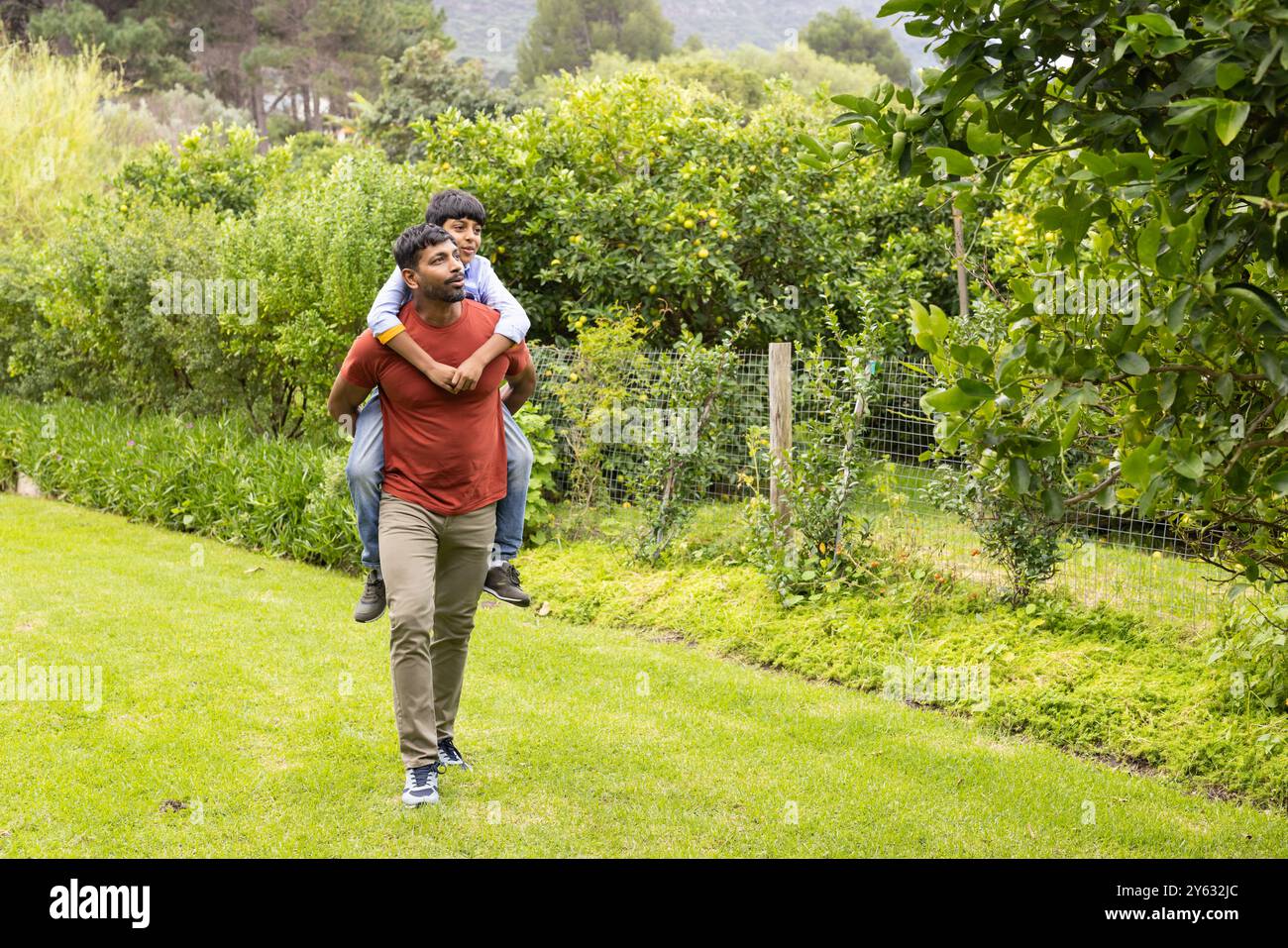 Indian father giving son piggyback ride while walking in lush green ...