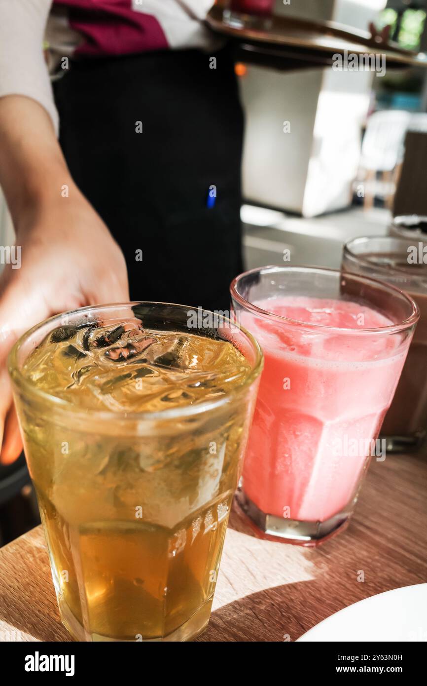 Tea and pink strawberry milk drinks served in glasses by waitress in a ...