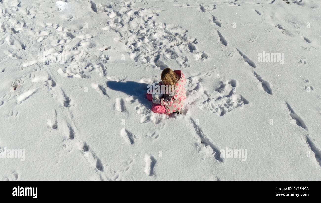 Funny little girl makes snowball sitting on snowy ground Stock Photo ...