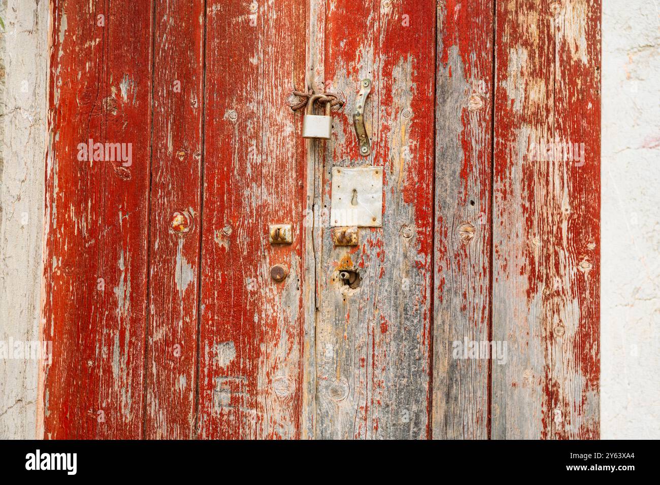 Rustic, flaking, peeling red paint on a rotting and decaying door with rusty lock and keyhole at ...