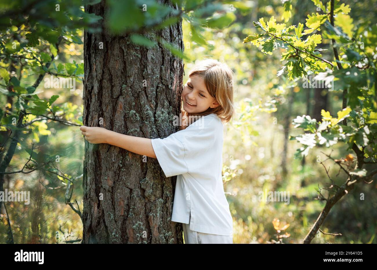 A teenage girl hugs a tree in the forest. Hugging and touching trees to ...