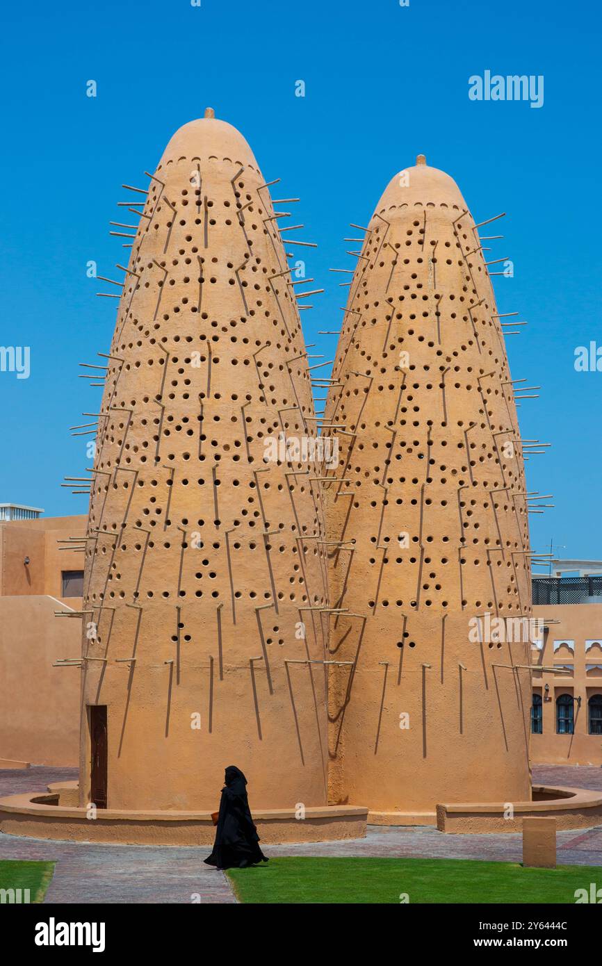 A woman in traditional black chador (garment) walking past the pigeon towers at the Katara ...