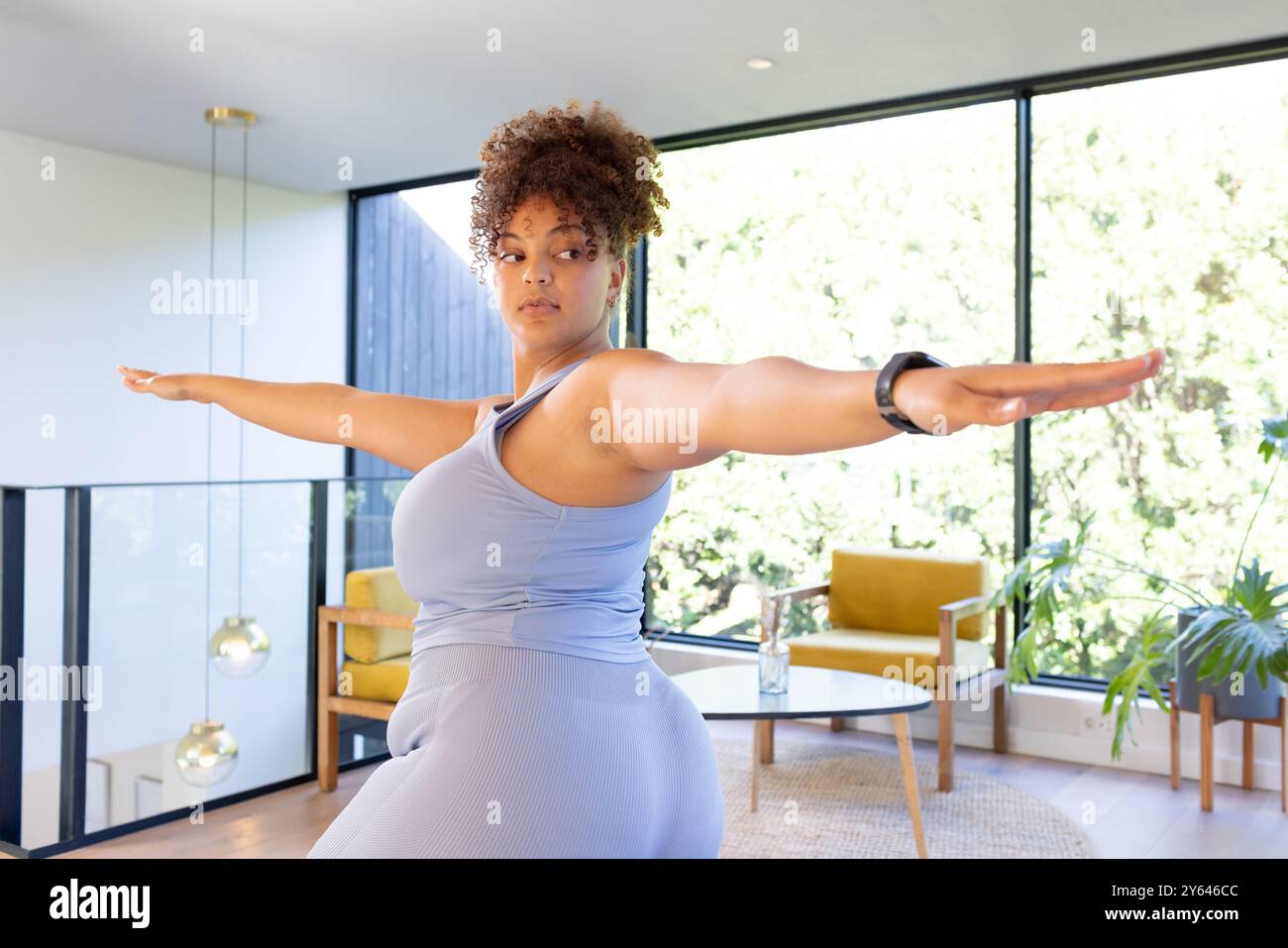 Practicing yoga, plus size woman stretching arms in modern living room ...