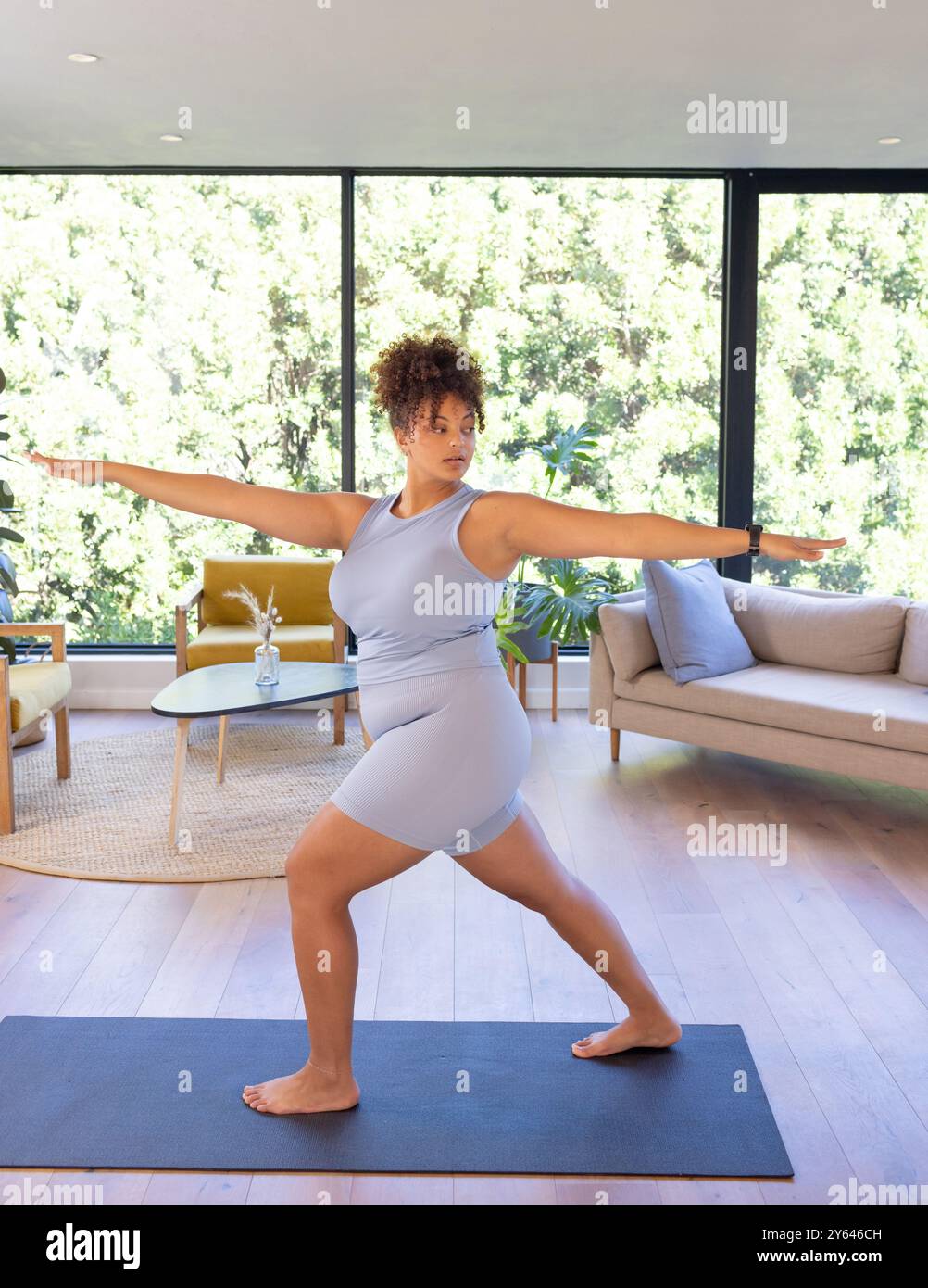 Practicing yoga, plus size woman in warrior pose on yoga mat indoors ...