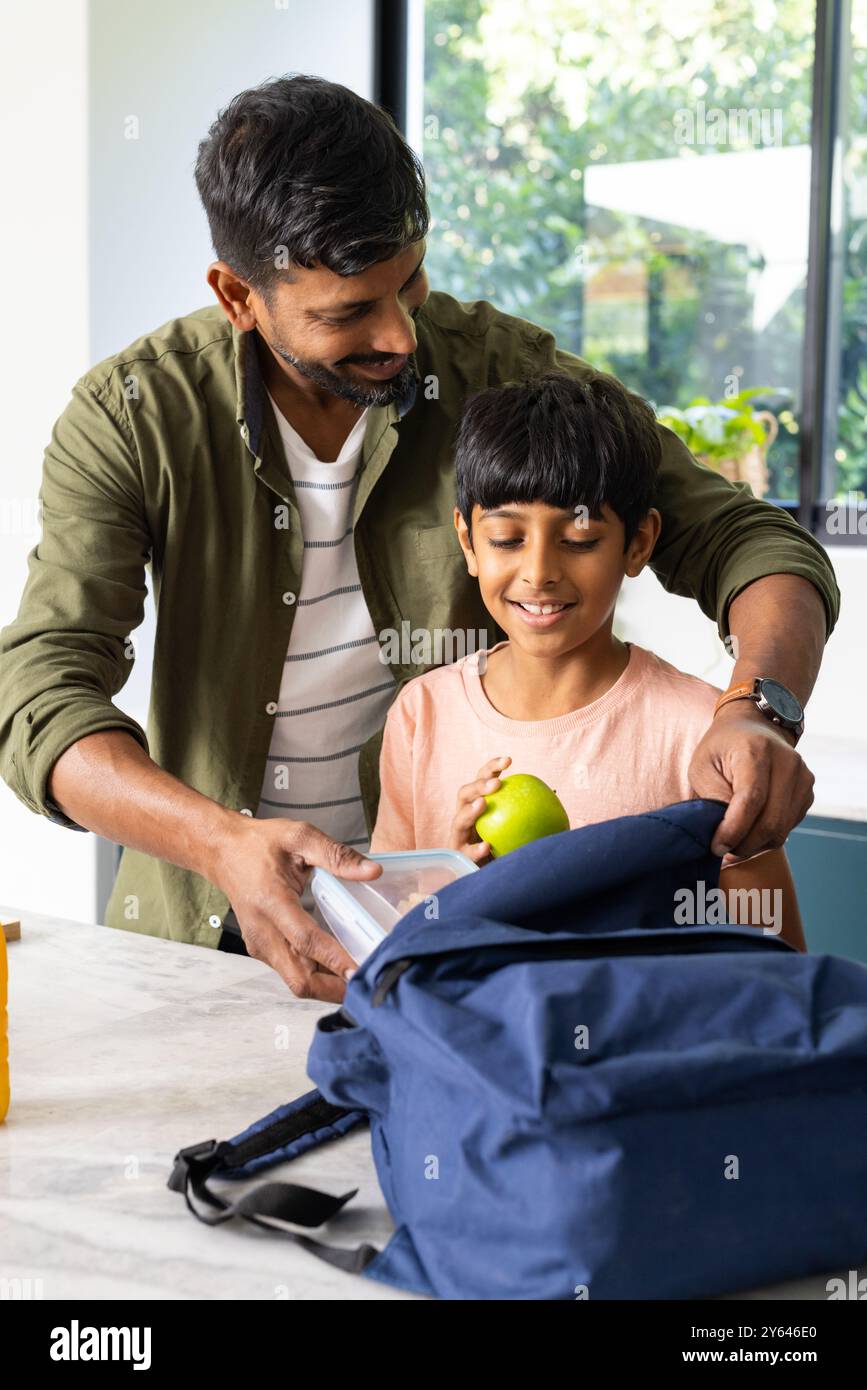 Packing school backpack, indian father helping son with lunch and books ...