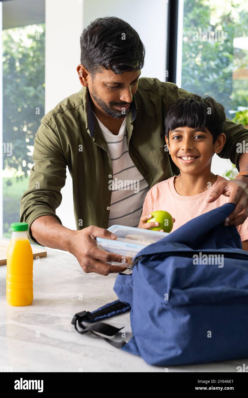 Packing school bag, indian father helping son with lunchbox and juice ...