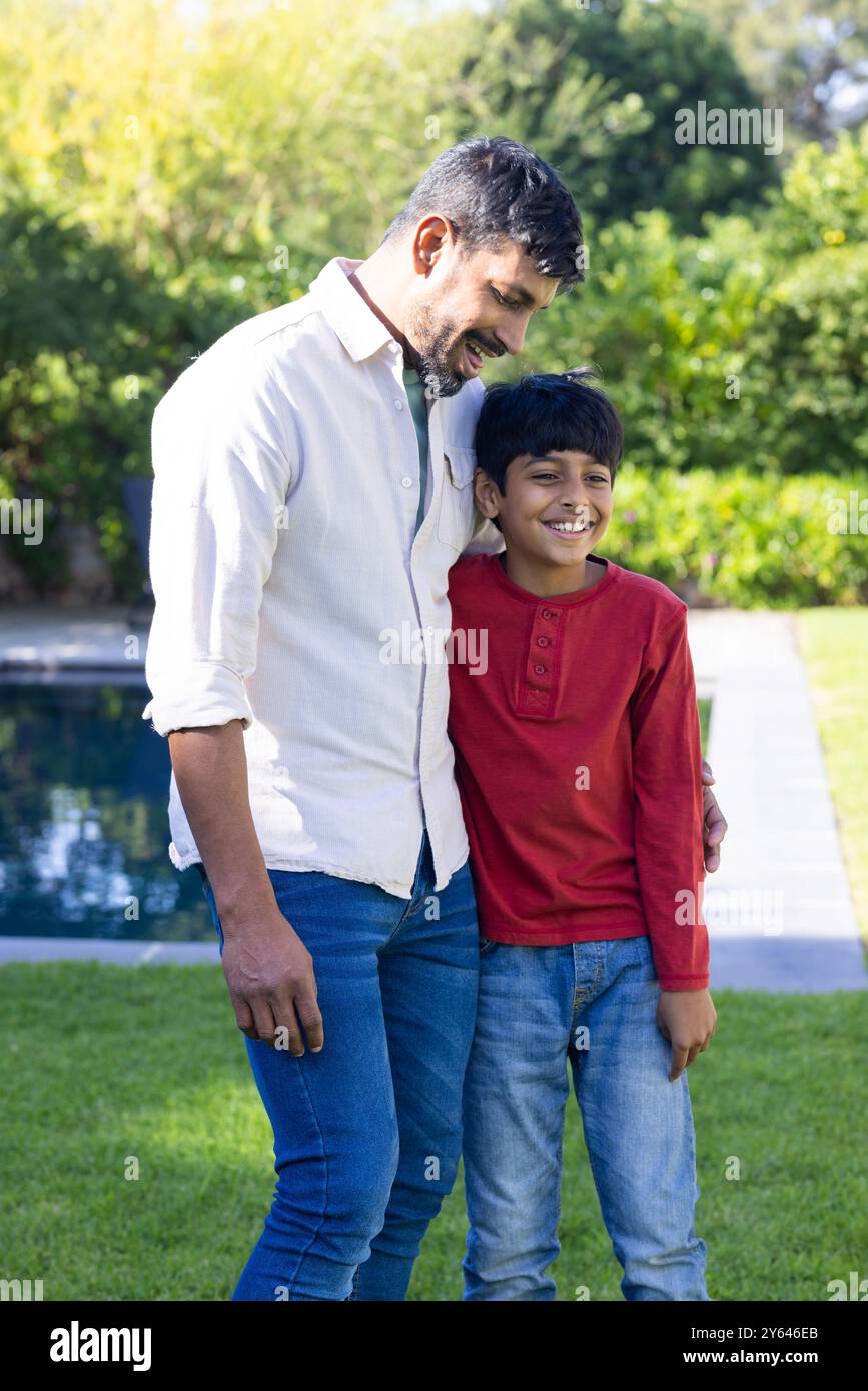 indian father and young son standing together outdoors, smiling and ...