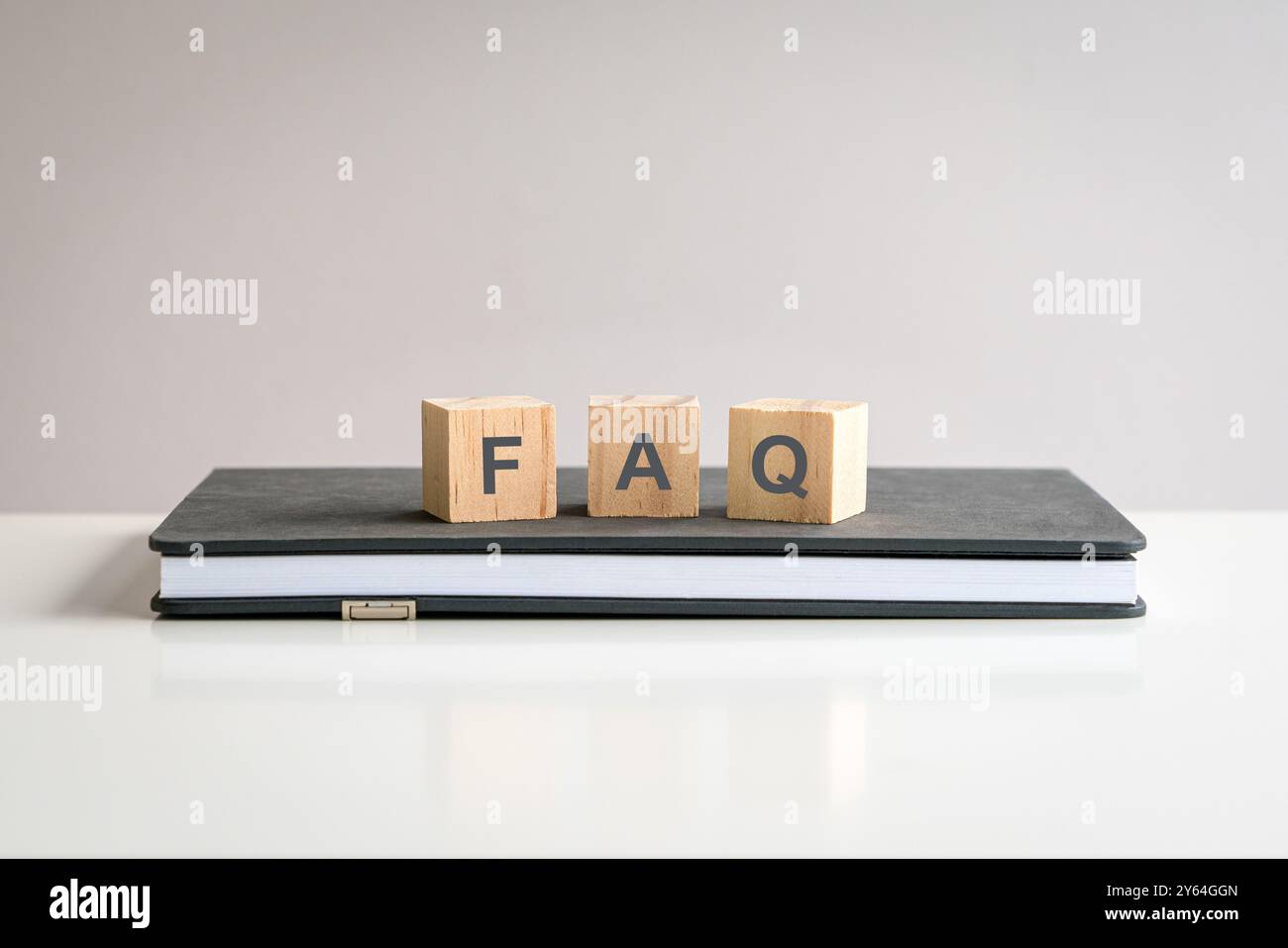Text FAQ on wooden blocks on top of a notepad of a white color table ...