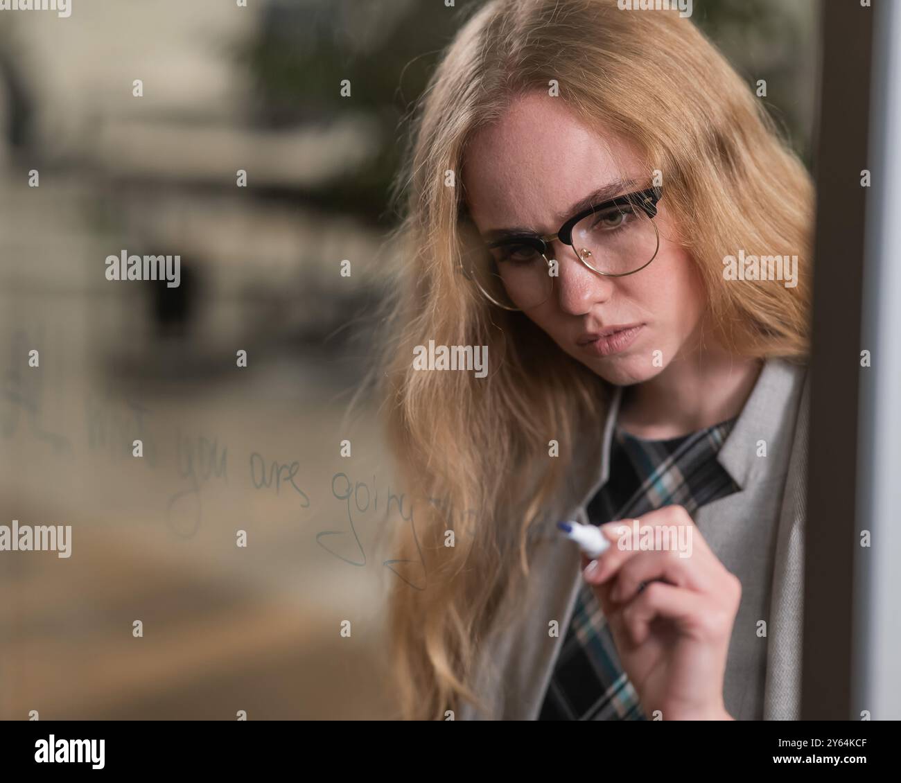 Caucasian woman with glasses writes text in English on a glass wall ...