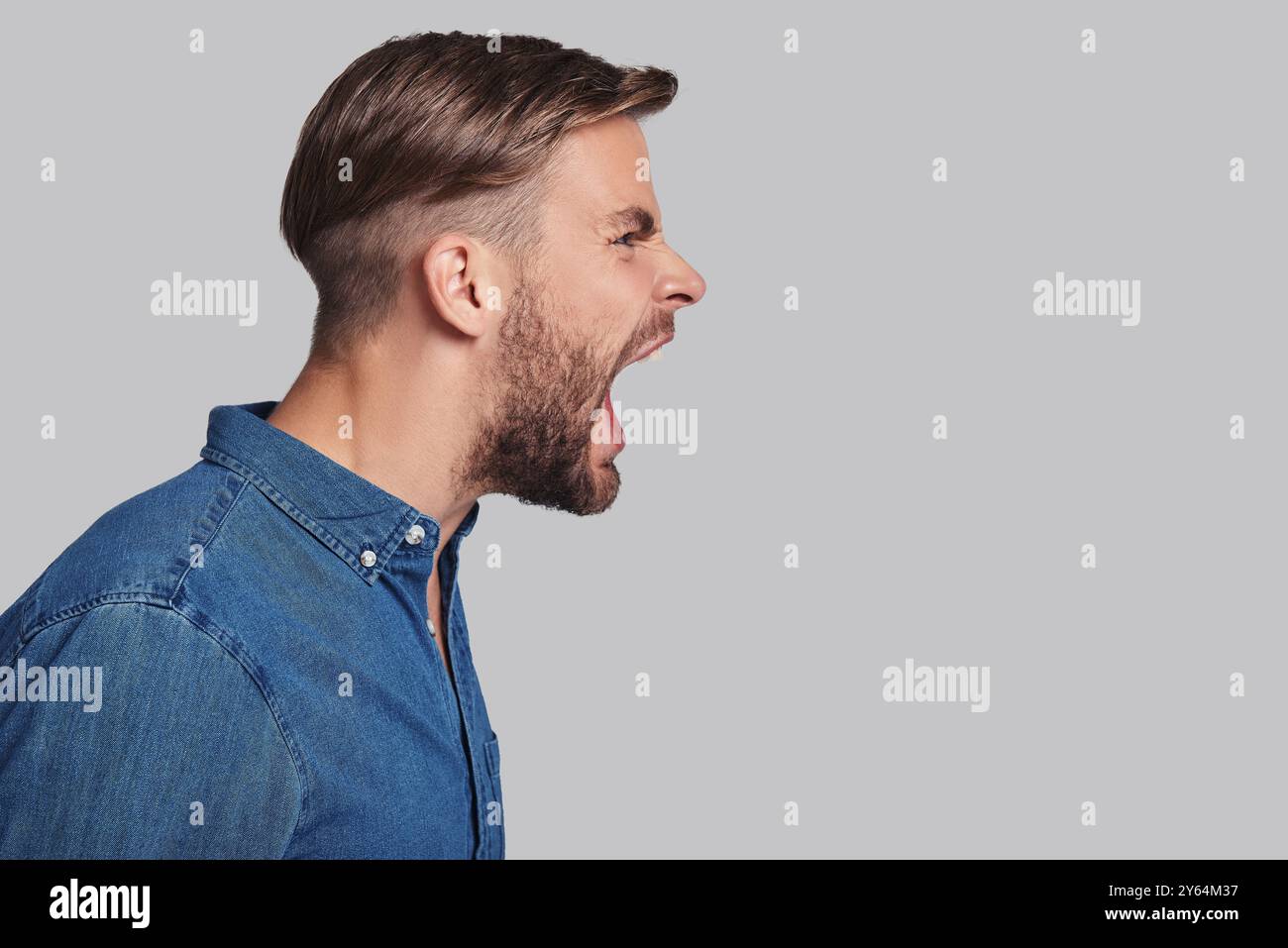 Feeling angry. Side view photo of young man screaming while standing ...