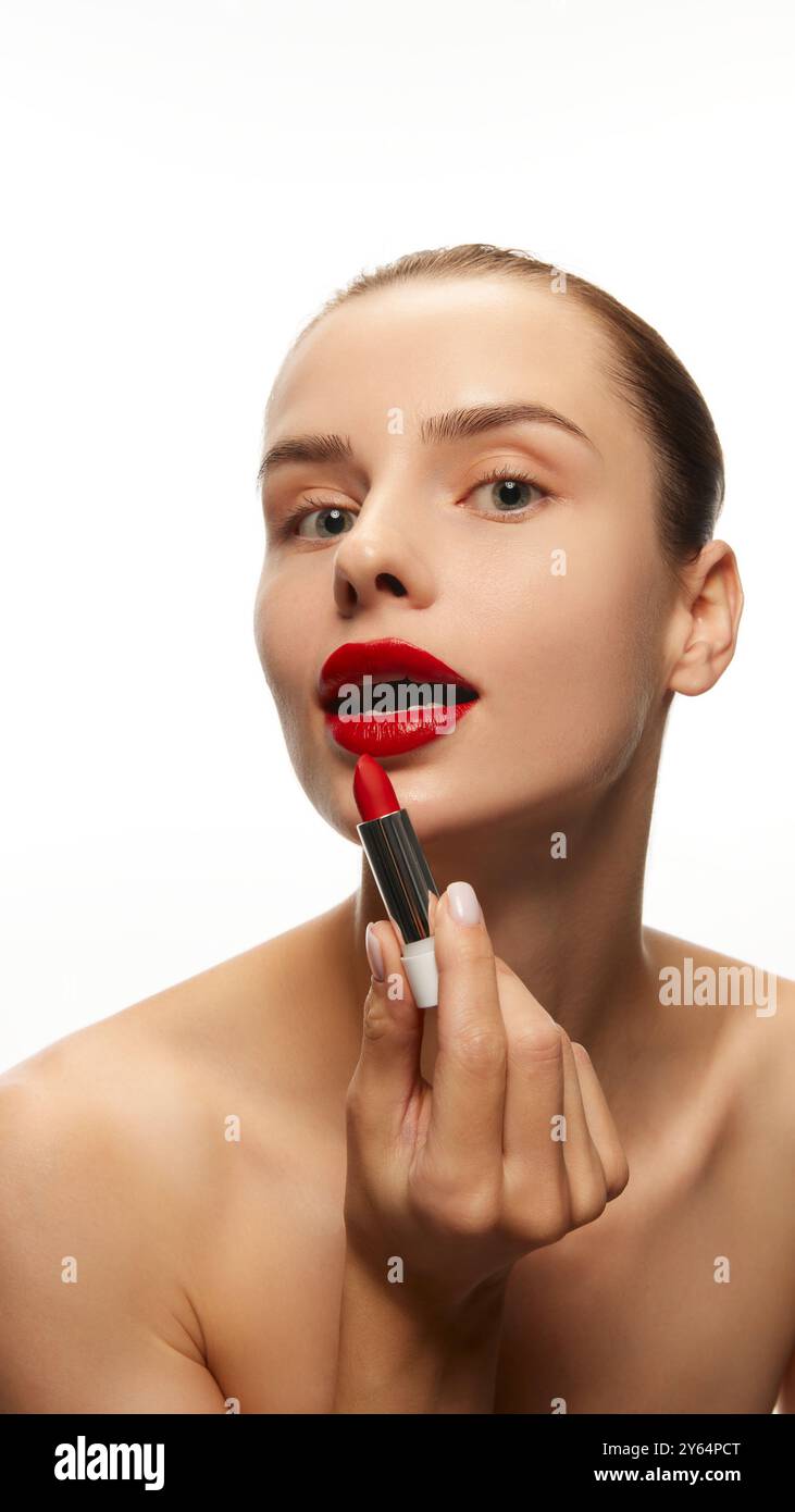 Portrait of young beautiful woman applying red lipstick, doing makeup ...