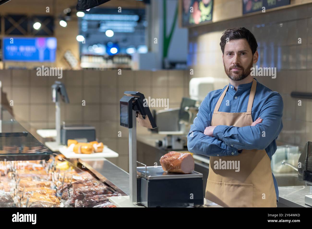 Butcher stands confidently behind counter in grocery store apron clad ...