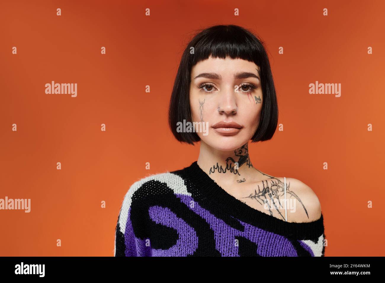 A young woman wears a bright sweater and shows off her tattoos while ...