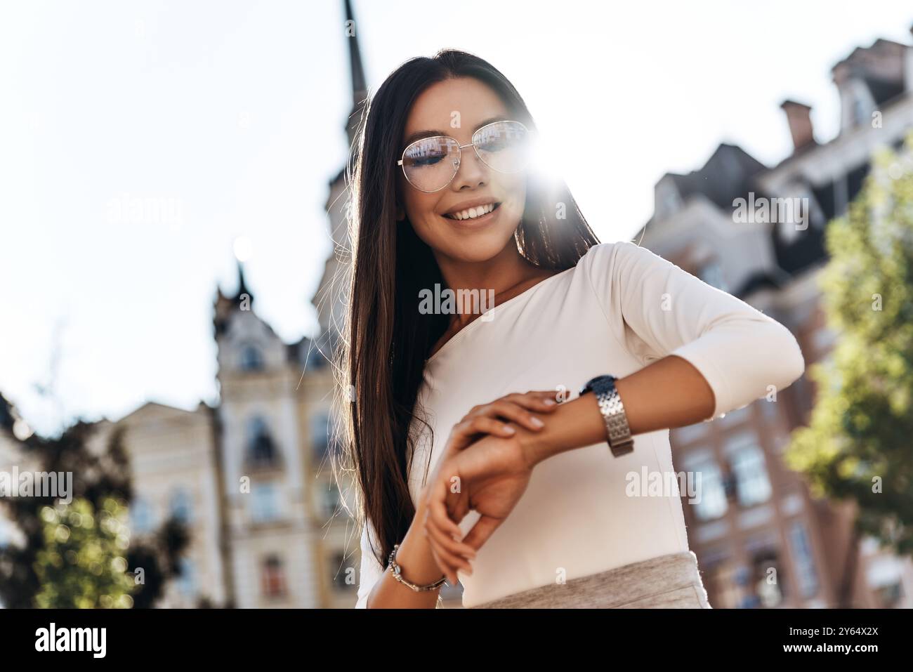 Time to go! Attractive young woman looking at her watch and smiling ...