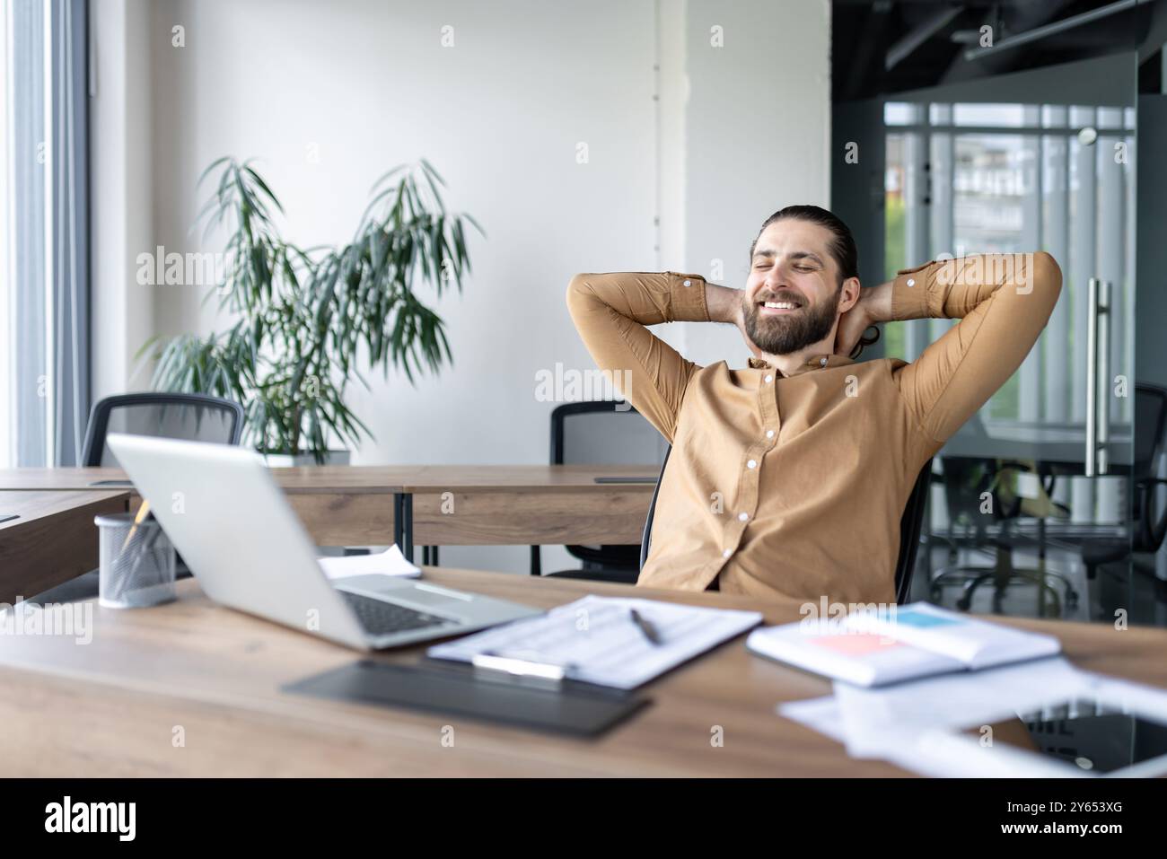 Businessman relaxing in office with hands behind head. Modern workspace ...