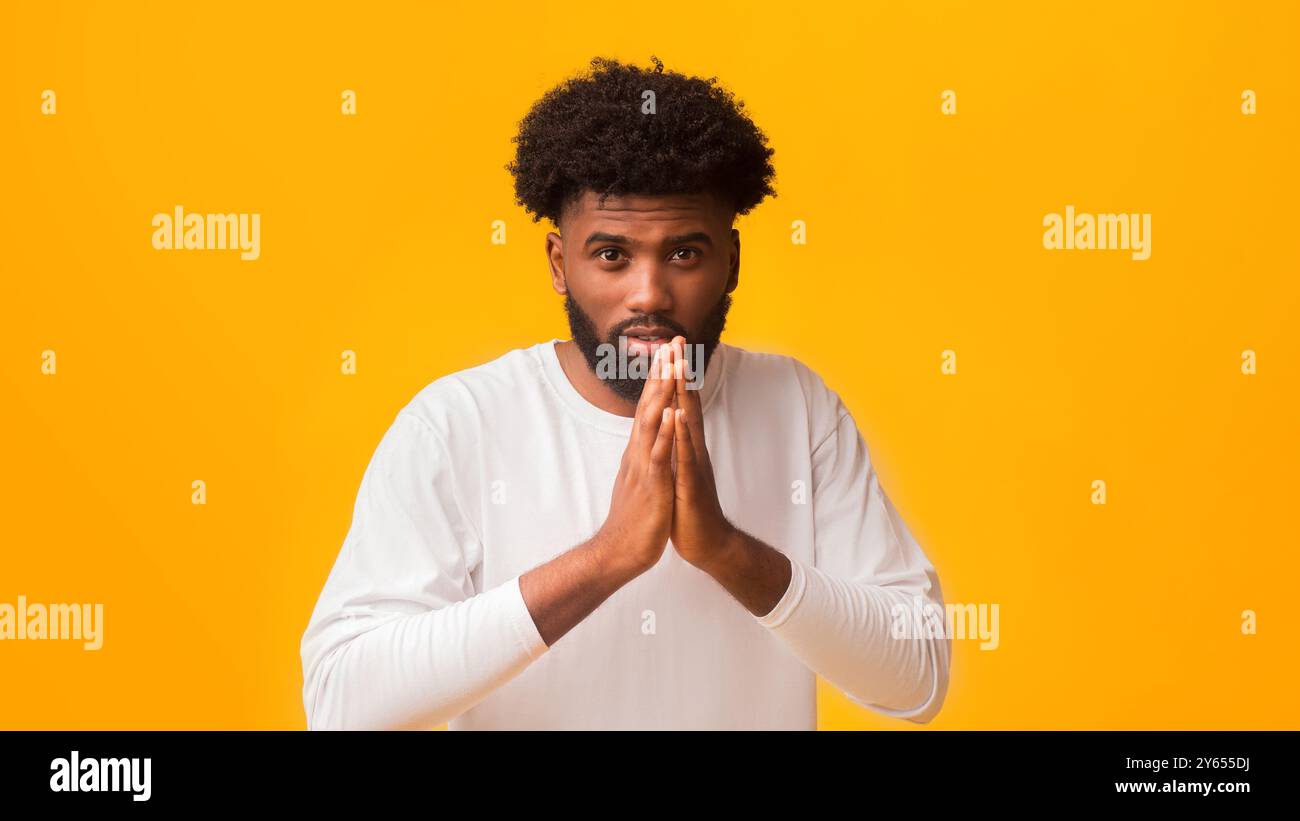 Serious black man praying over orange background Stock Photo - Alamy