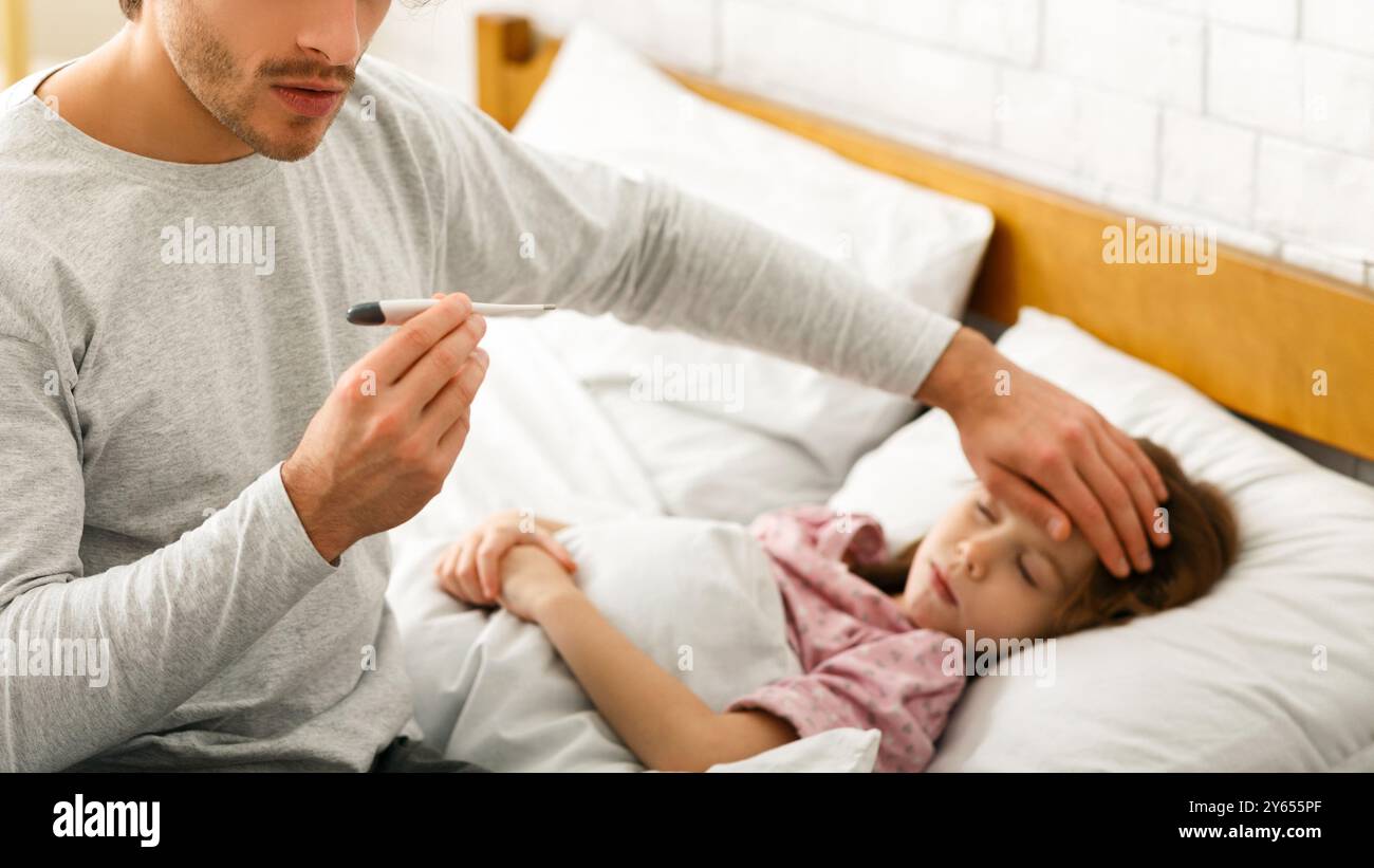 Father checking his daughter's temperature with thermometer in bed ...